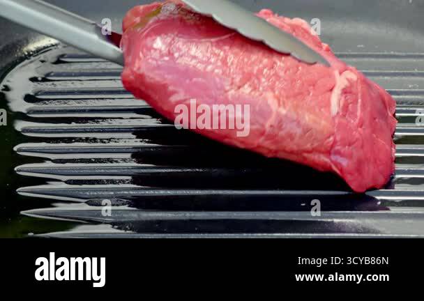 Food preparation. A chef places a raw piece of steak on a cast iron ...