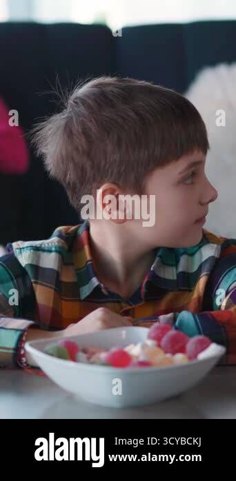 Young cheerful kid eating delicious sugar candies by table in living ...