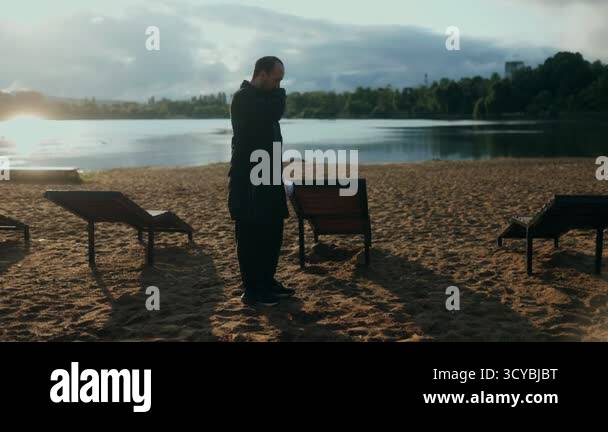 At sunrise on a remote beach, a man in dark clothing stands alone ...