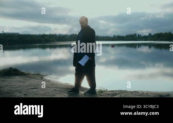 A distressed man reads a painful letter alone by the lake. His furrowed ...