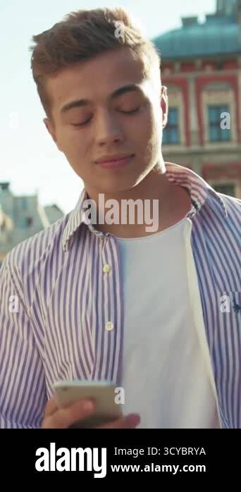 Smiling young happy man walk on street use phone look around sunlight ...