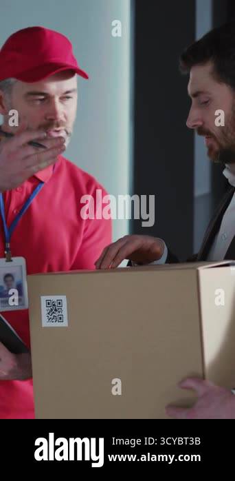 A suited man carries a box in a delivery hub. Another man checks his ...