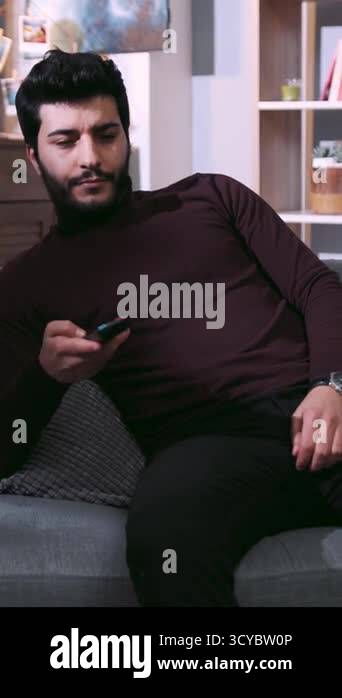 In this cozy living room, a bearded man relaxes on a comfy couch, using ...