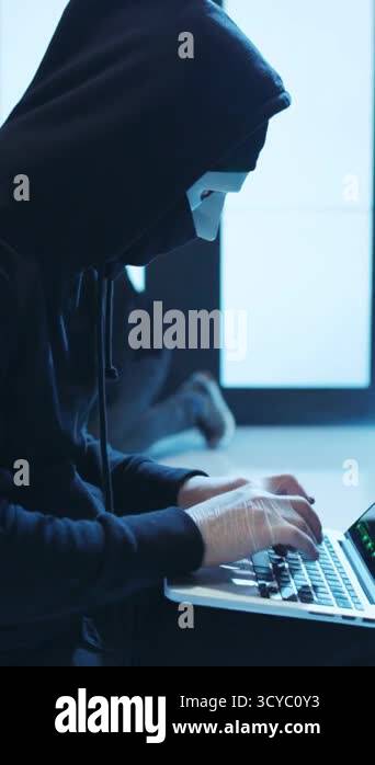 A mysterious hacker, with a masked face, is intensely typing on a ...