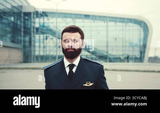 Good-looking caucasian pilot leaves the airport, holds his dress cap in ...