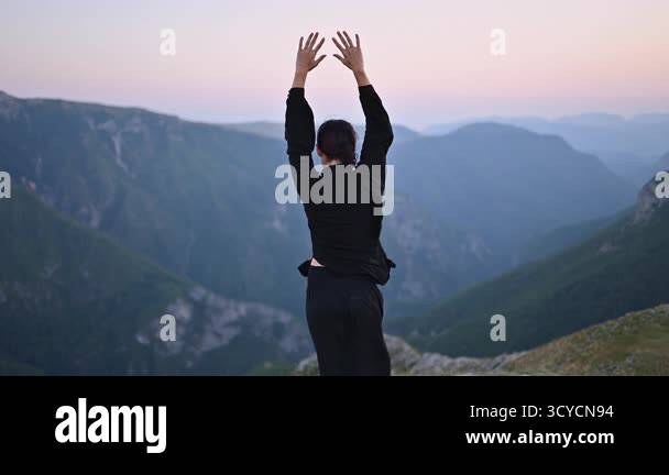 A woman practicing Tai Chi in a traditional black outfit on a mountain ...