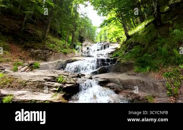 Aerial video of a beautiful waterfall flowing over rocks in lush green ...