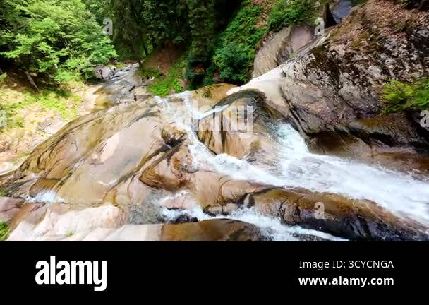 Aerial video of a beautiful waterfall flowing over rocks in lush green ...