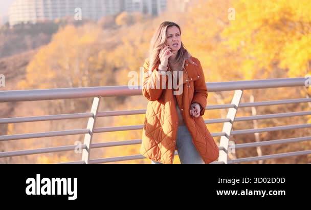 Woman in coat argues emotionally while talks on smartphone on bridge in ...