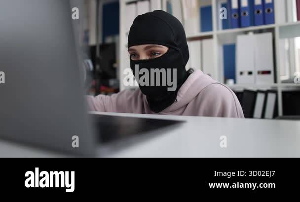 Female thief in ski mask looks at laptop screen through magnifying ...