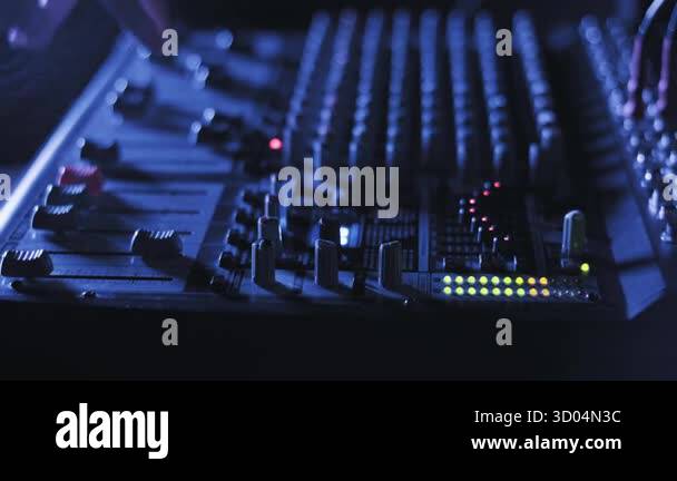 Low-angle shot of a sound engineer adjusting faders on a mixing console ...
