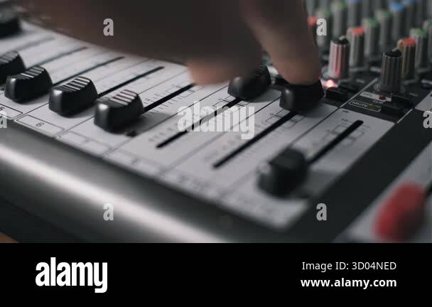 Angled side view of an engineers hand pulling down two faders on a ...