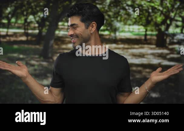 Man shows open palms with raised forearms in sunlit green forest park ...