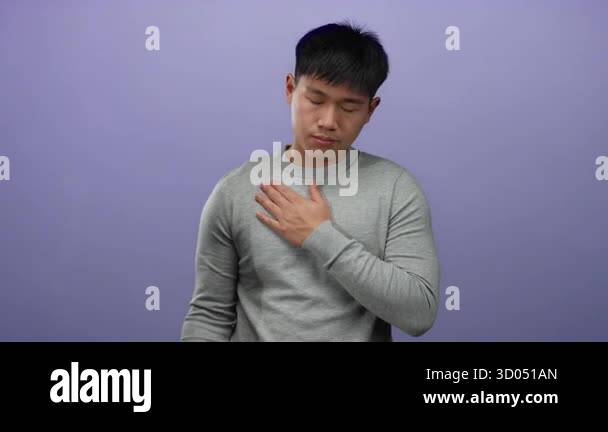 Young chinese man in gray sweater gestures sincerely with hand on heart ...