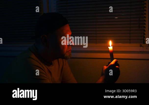 Blackout, No electricity. Man in a dark room near a window with candle ...
