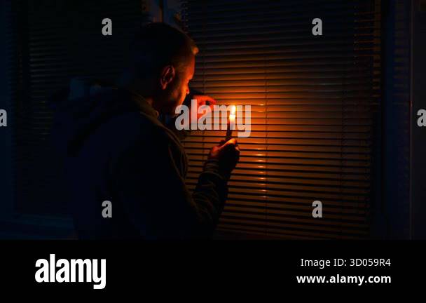 Blackout, No electricity. Man in a dark room near a window with candle ...