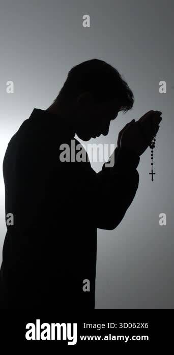 Vertical video silhouette of a man praying with hands clasped, holding ...