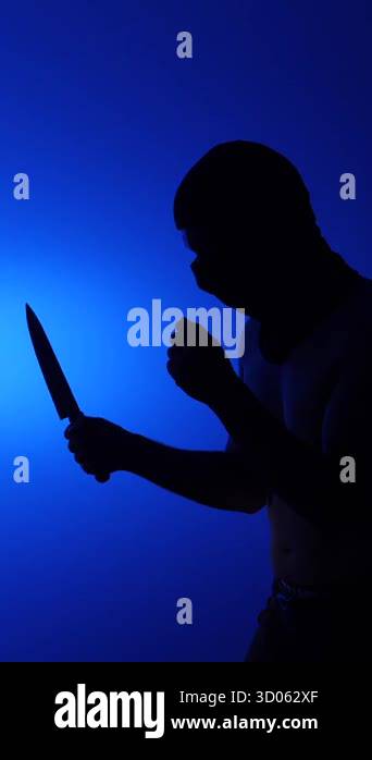 Vertical video hooded silhouette of a man holding a sharp knife in a ...