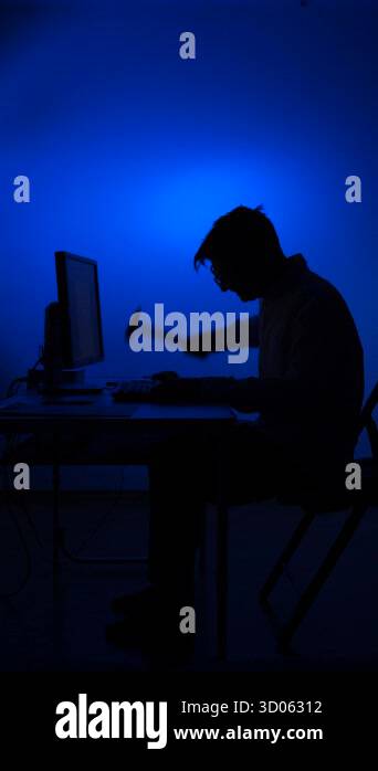 vertical video Man in silhouette sitting at a desk, angrily smashing a ...