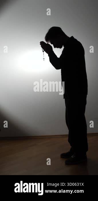vertical video Man silhouette kneeling in prayer, holding a rosary ...