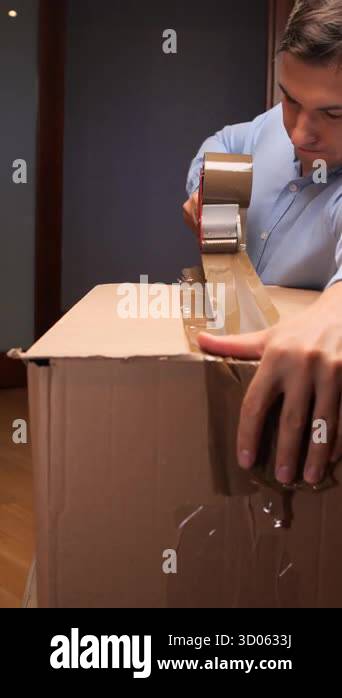 vertical video Man securing a cardboard shipping box with an adhesive ...