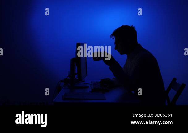 Man in silhouette working on a desktop computer, drinking coffee in a ...
