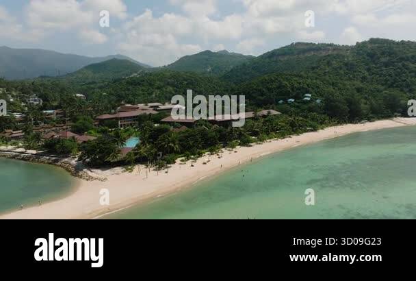 Resort area on the beach with clear water, surrounded by green hills ...