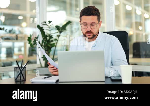 Focused businessman in a light blue shirt attentively reviews documents ...
