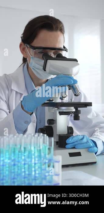 Female scientist wearing protective glasses and mask using microscope ...