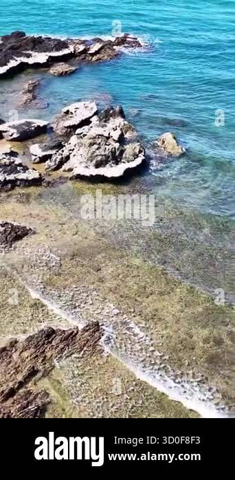Drone camera glides above a sunlit, rocky coastline with turquoise ...