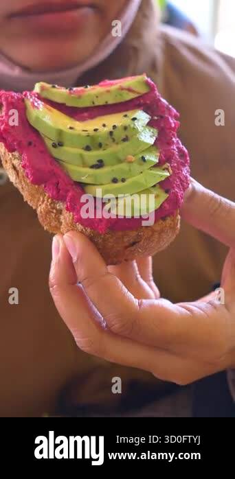 Sliced avocado on beetroot spread atop bread enjoyed in a cozy cafe ...