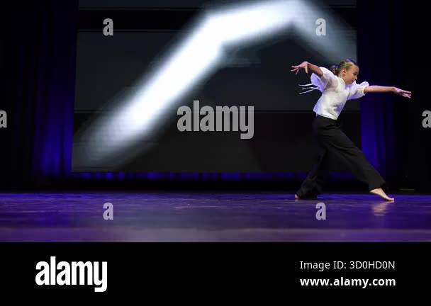 A young dancer performs contemporary moves on a dim auditorium stage ...