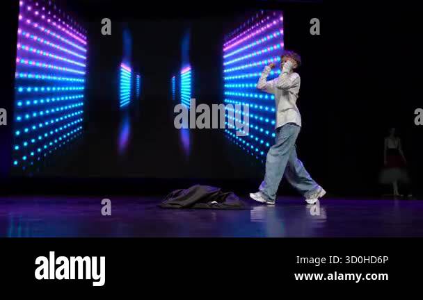 A young male dancer in a white 84 shirt and jeans performs hip hop ...