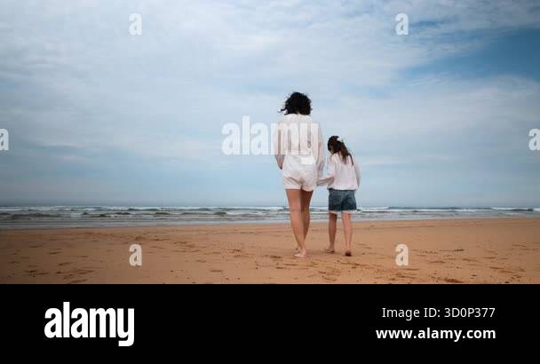 An adult mother and her girl daughter walk hand in hand toward the ...