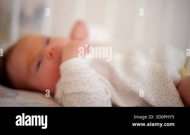 A newborn baby in soft pajamas moves gently in a crib, stretching tiny ...