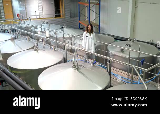 Female brewmaster in a white lab coat walking and inspecting large ...