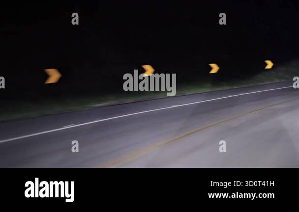 Curving country road with yellow chevron signs at night, illuminated by ...