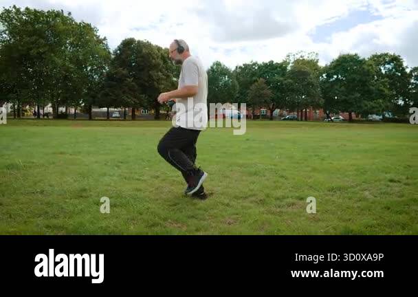 Man dancing happily in park wearing headphones. Adult man feeling ...