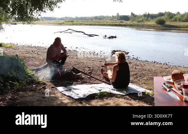 Man and woman lighting a fire to prepare a barbecue outdoors. Picnic ...