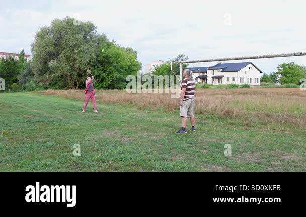 Two people playing badminton on a field near old football goalposts ...