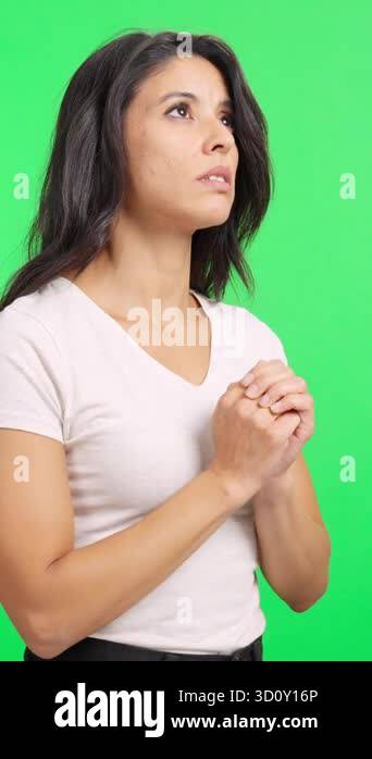 Faithful woman praying with folded hands and hopeful expression against ...