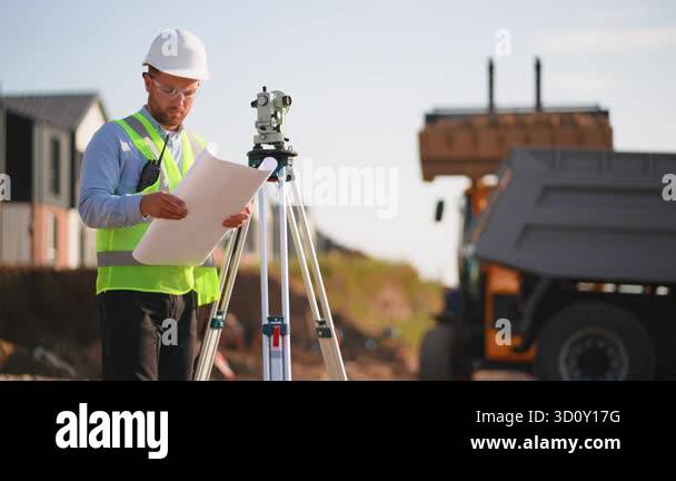 Caucasian man surveyor in a hard hat and safety vest using a theodolite ...