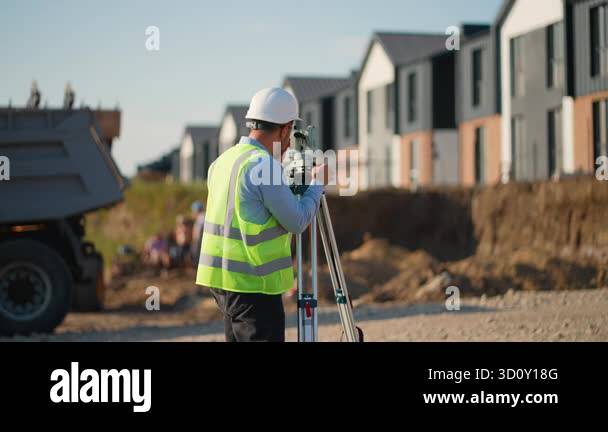 Professional land surveyor in a hard hat and safety vest using a ...