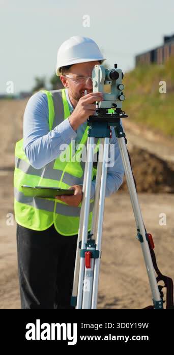 Caucasian man in a hard hat and safety vest working as a land surveyor ...