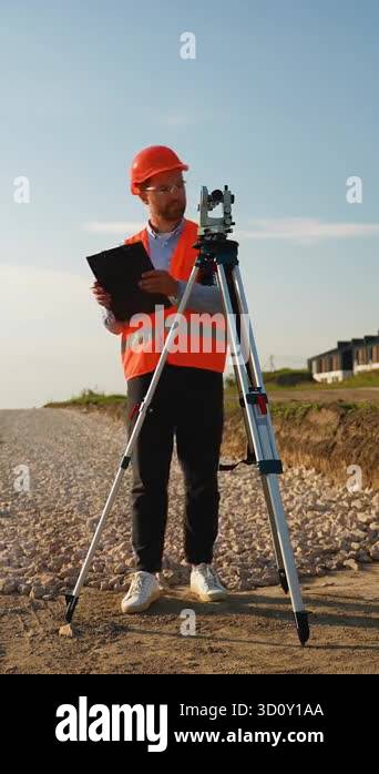 Male surveyor wearing a hard hat and safety vest working with a ...