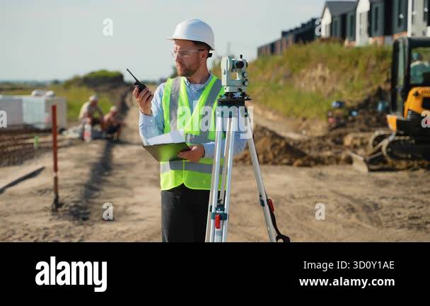Professional land surveyor in a hard hat and safety vest working with a ...