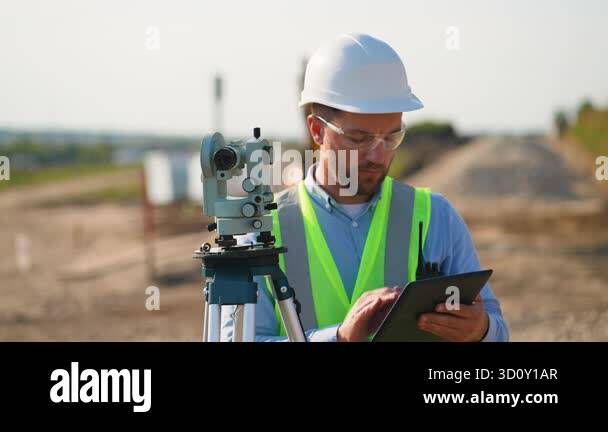 Caucasian land surveyor in a hard hat and safety vest using a ...