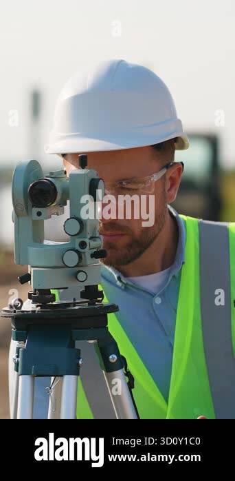 Caucasian land surveyor wearing a hard hat and safety vest using a ...