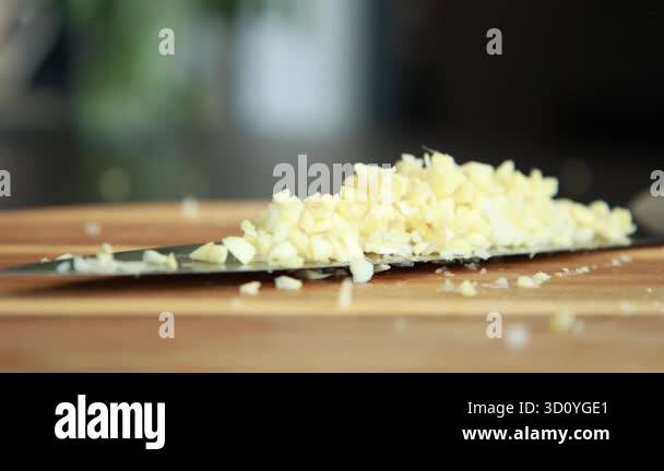 Fresh garlic cloves being chopped and diced on a rustic wooden cutting ...