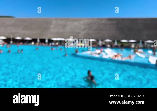 An outdoor pool area. People swim, relax in the water, and sunbathe ...